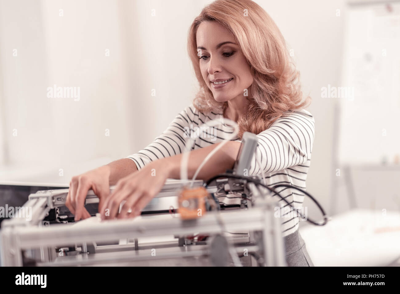 Pretty adult smiling woman adjusting 3D printer Stock Photo - Alamy