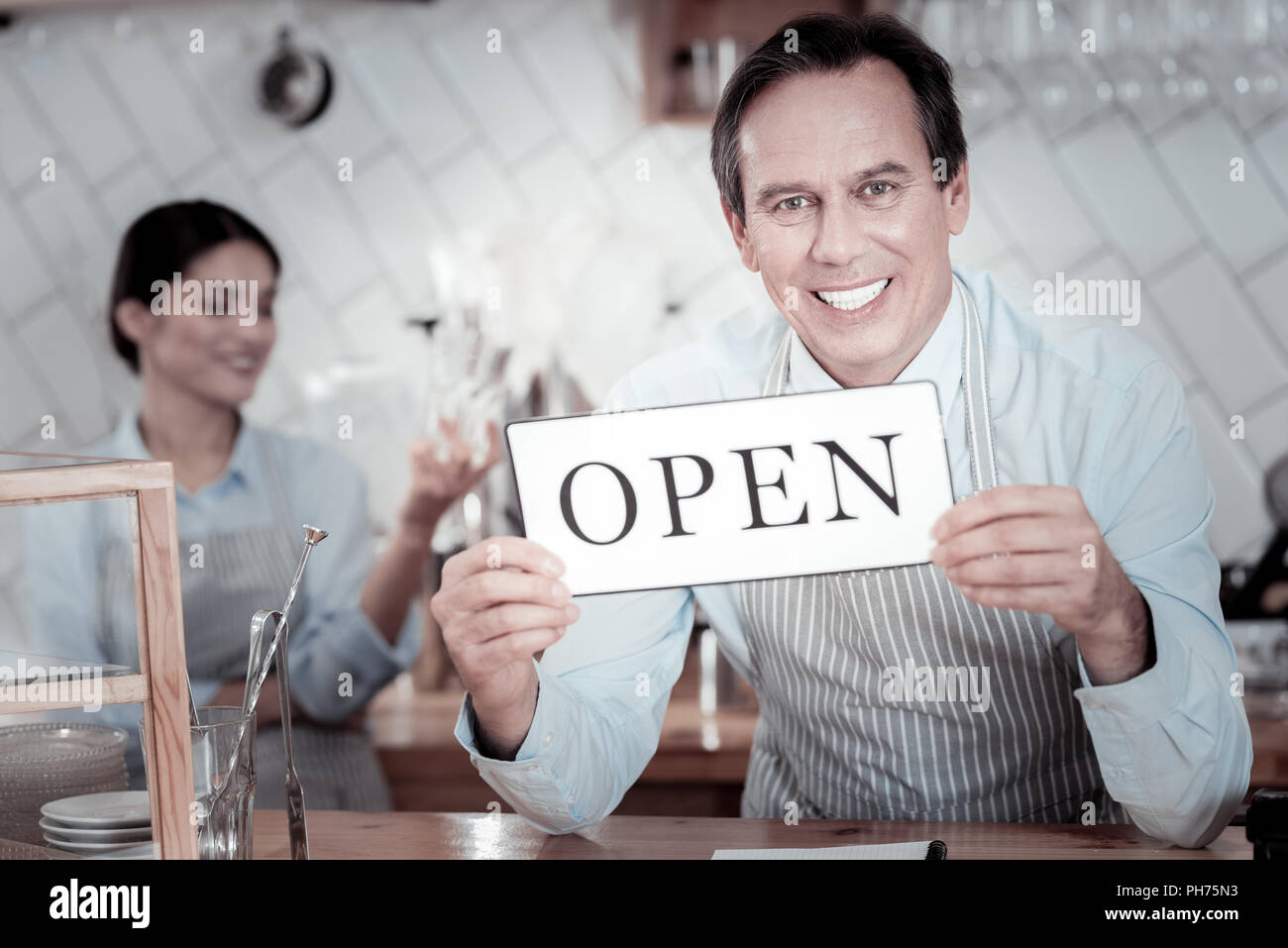 Excited waiter smiling and holding the open sign Stock Photo - Alamy