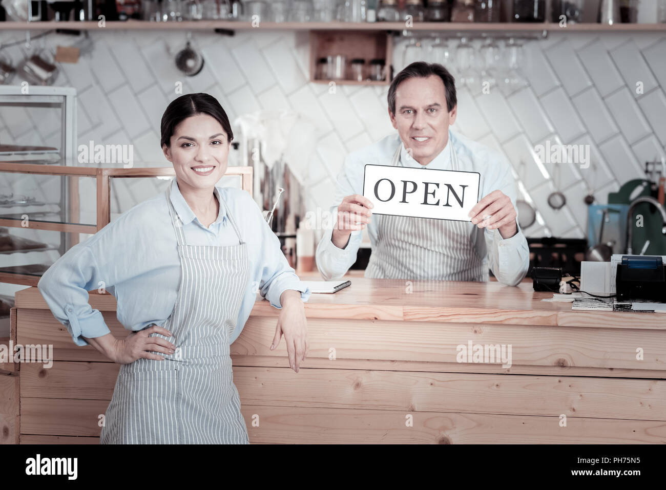 Smiling waiters standing near the bar counter and waiting for the first ...