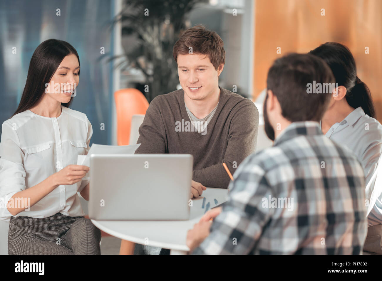 Positive young people sitting around the table Stock Photo - Alamy