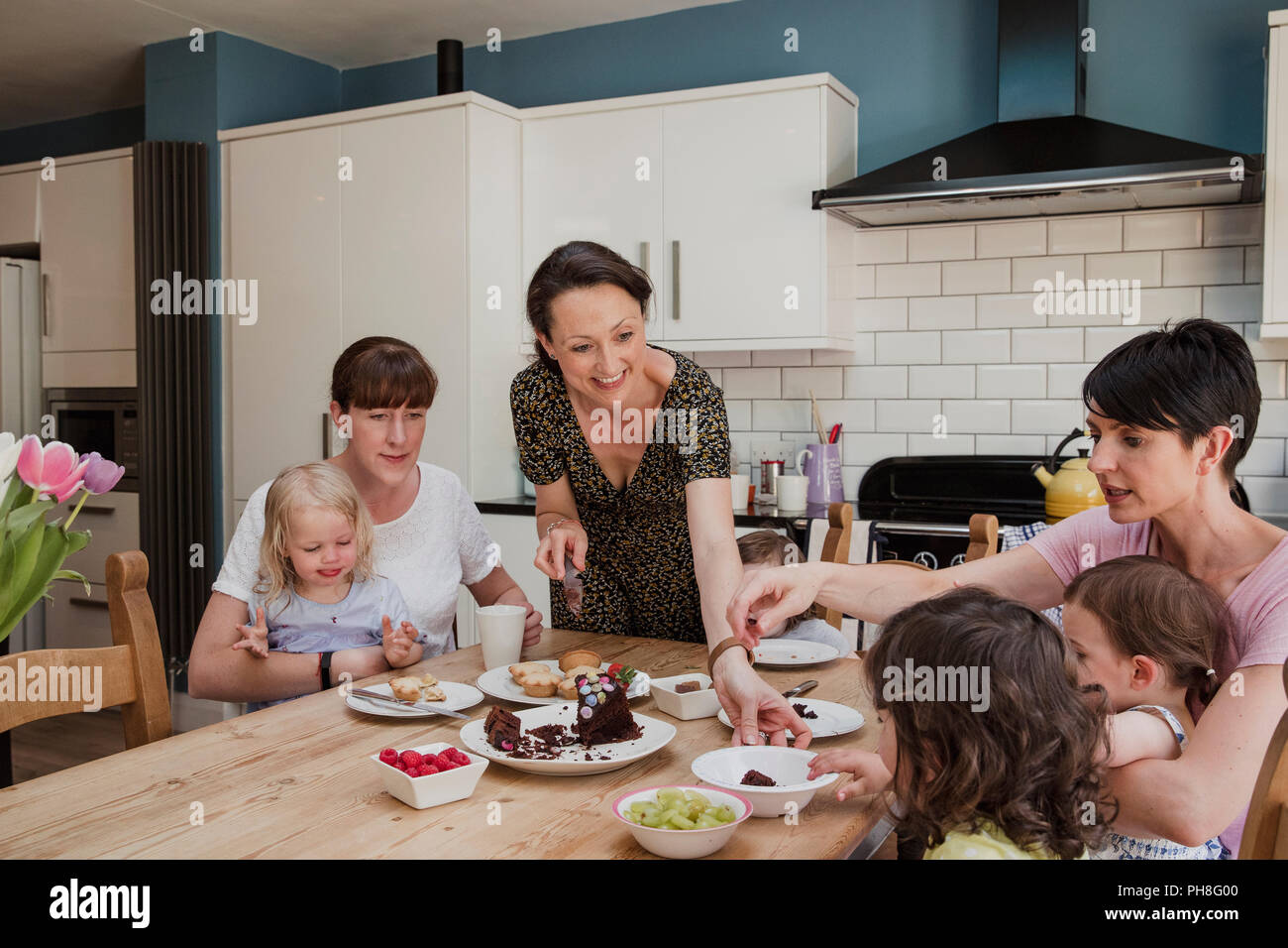 MId adult woman handing a slice of cake to a little girl sat at the ...