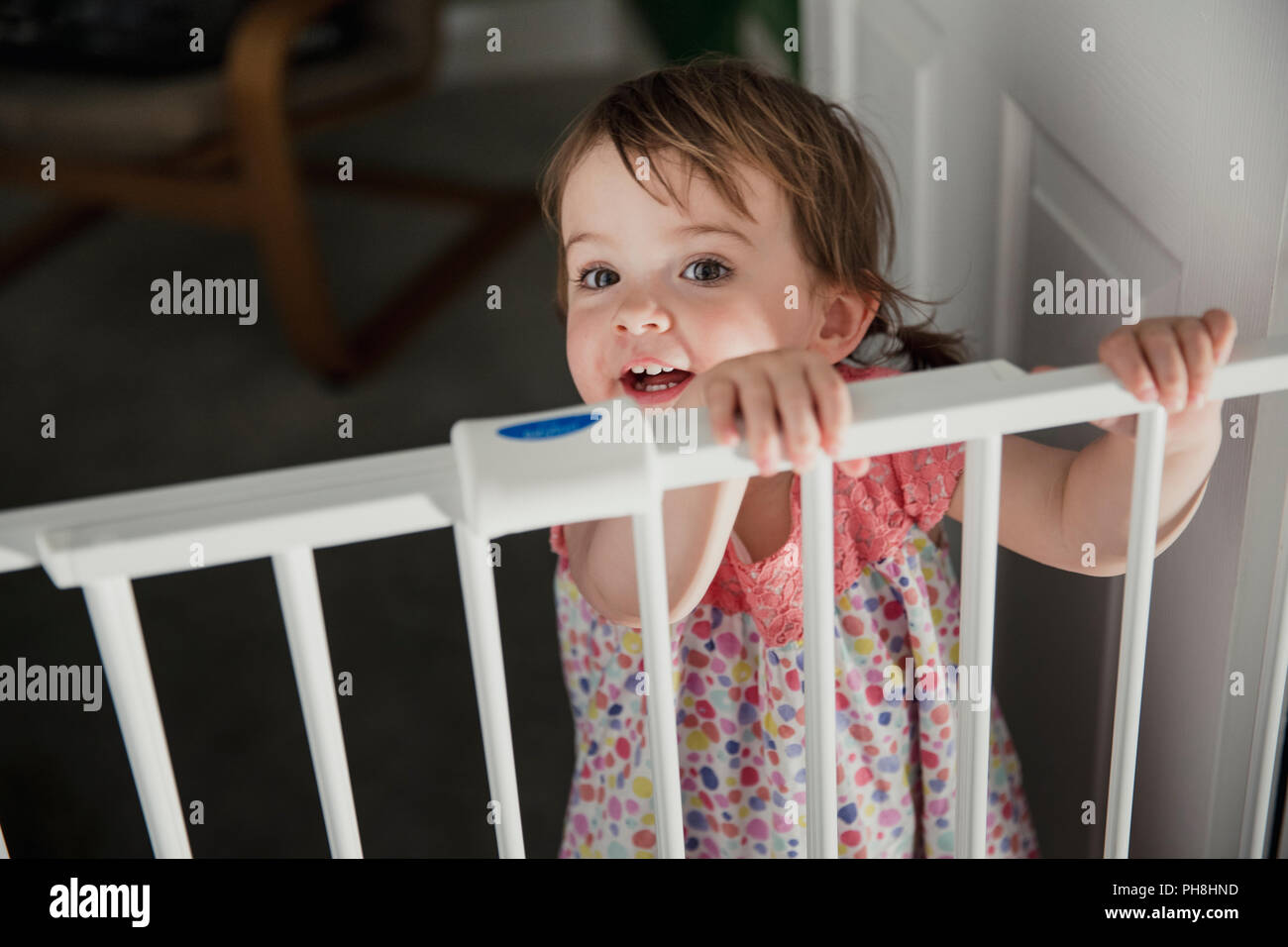 Front view of a little girl standing on the other side of a baby saftey ...