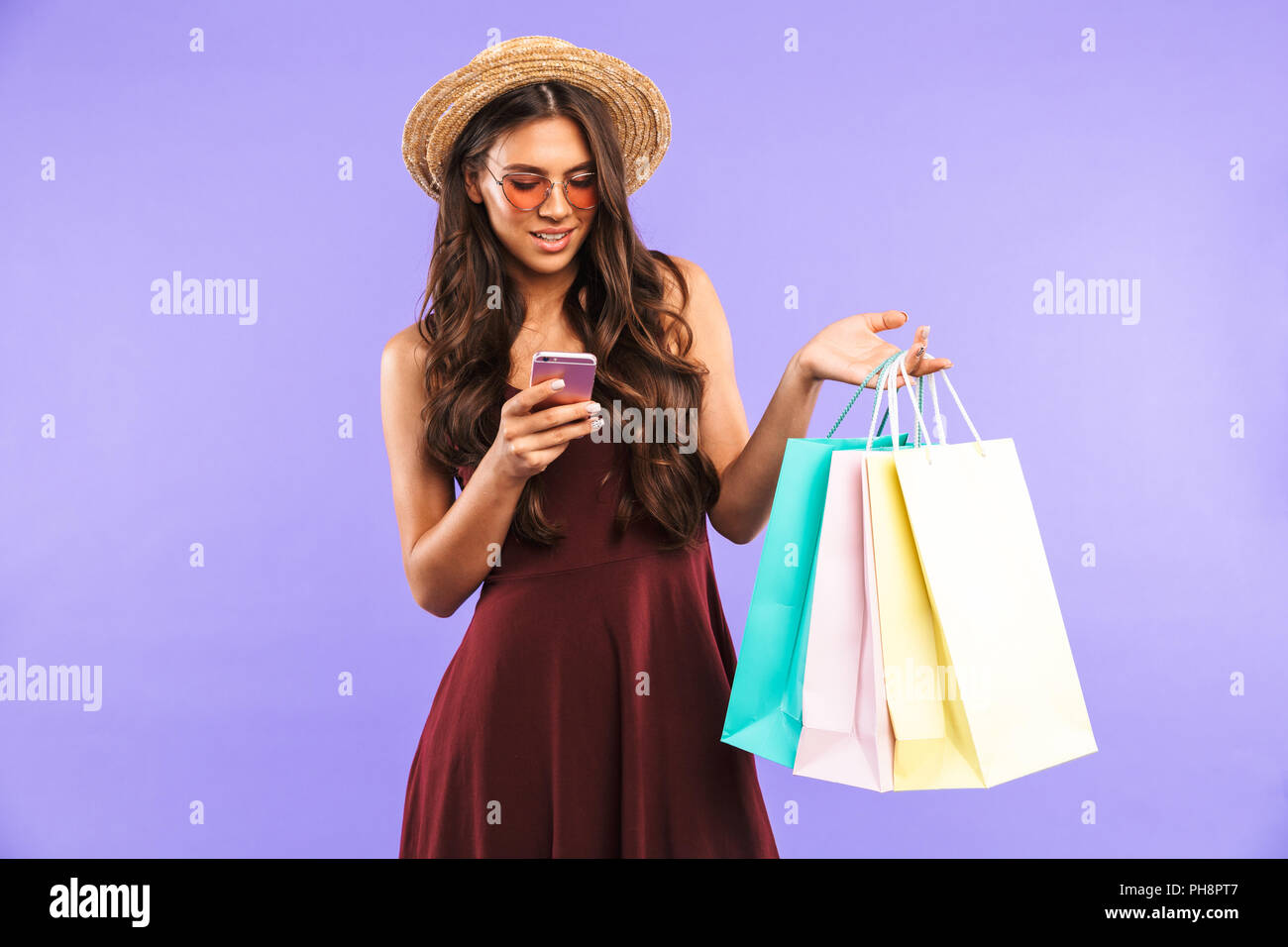 Portrait of a cheerful young woman in straw hat and sunglasses standing isolated over violet ...
