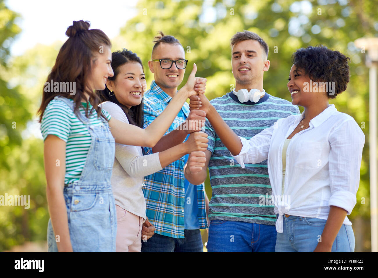happy friends making thumbs up gesture in park Stock Photo - Alamy