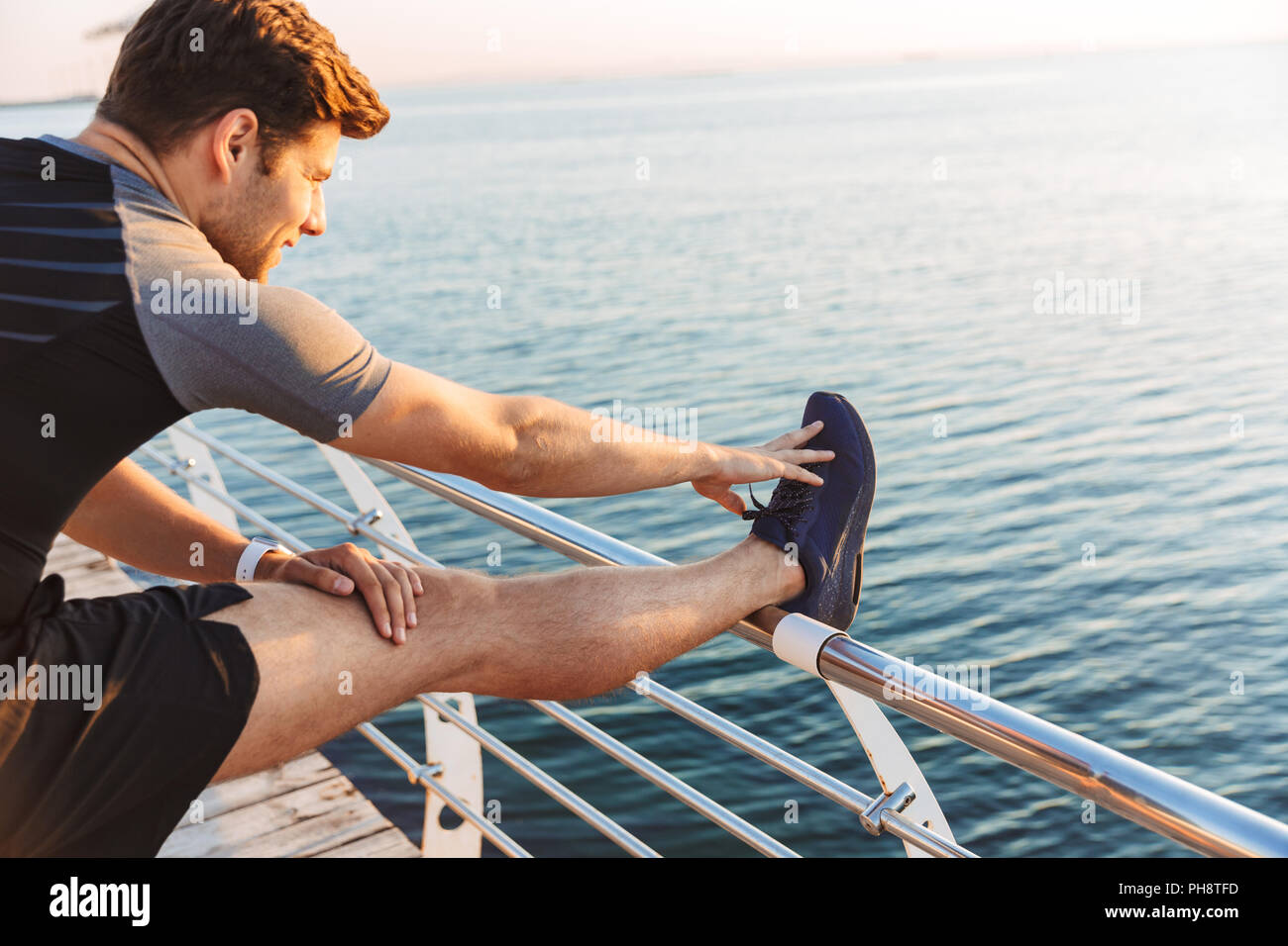 Image of young sporty man 20s in shorts and t-shirt raising leg on ...