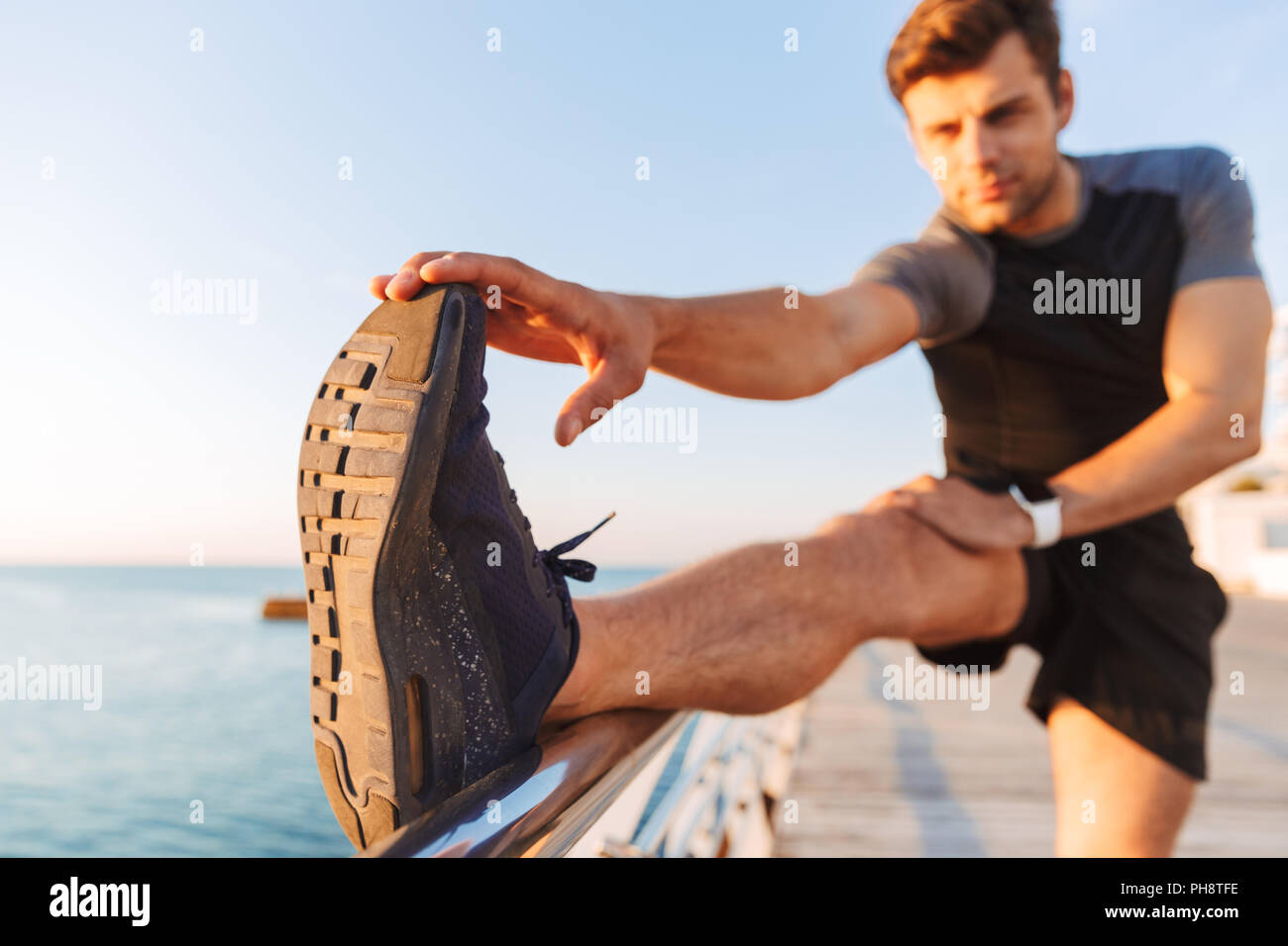 Photo of runner guy 20s in shorts and t-shirt raising leg on railing ...