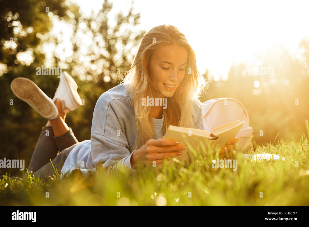 Portrait of a delighted young girl with backpack laying on a grass at ...