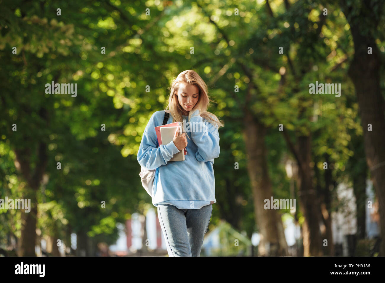 Lovely young girl student with backpack carrying books, walking at the ...