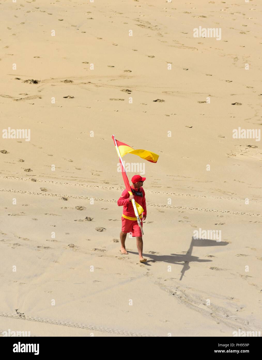RNLI lifeguard on duty carrying a red and yellow flag across the beach ...