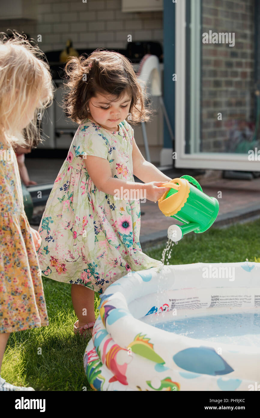 Side view of two little girls standing next to an inflateable pool. One ...