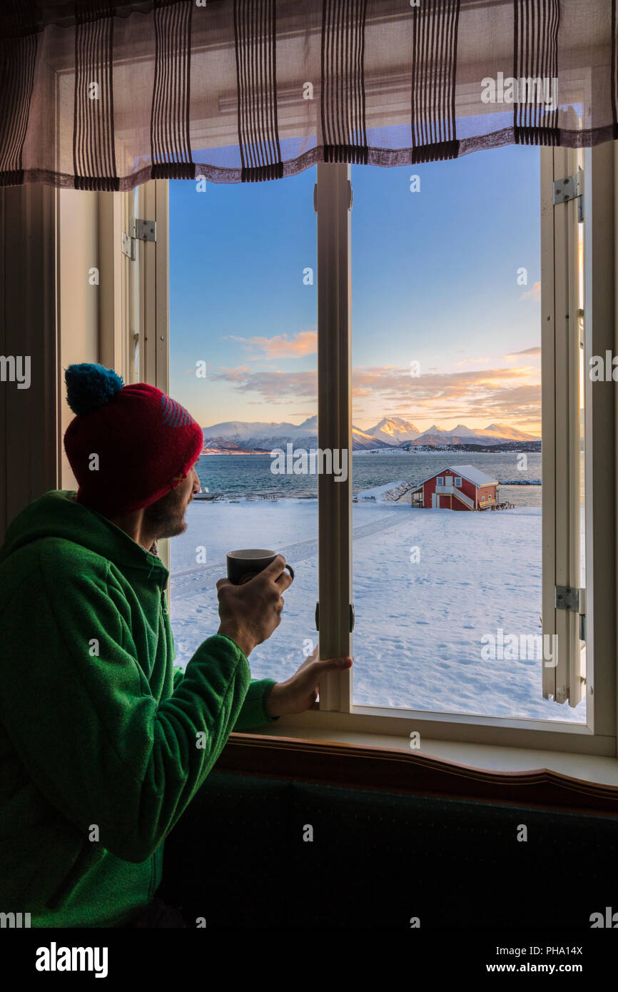 Man looks at the snowy landscape from a window, Troms, Norway ...