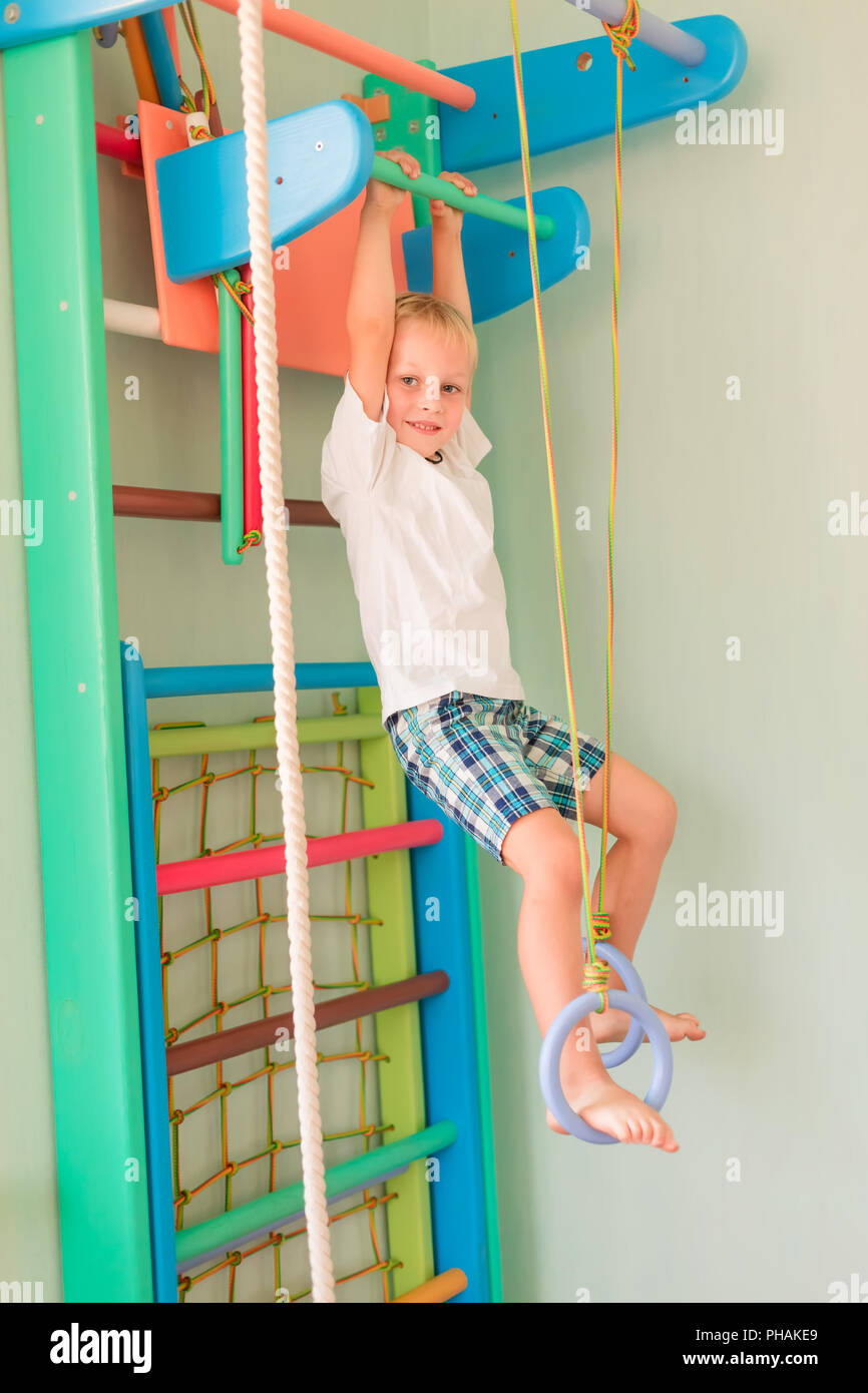 Happy little boy hanging on rings on home wall gym. Child's sportive ...