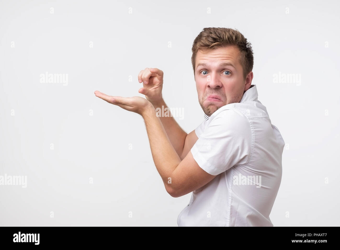 Positive handsome man shows something very tiny or small, being in ...