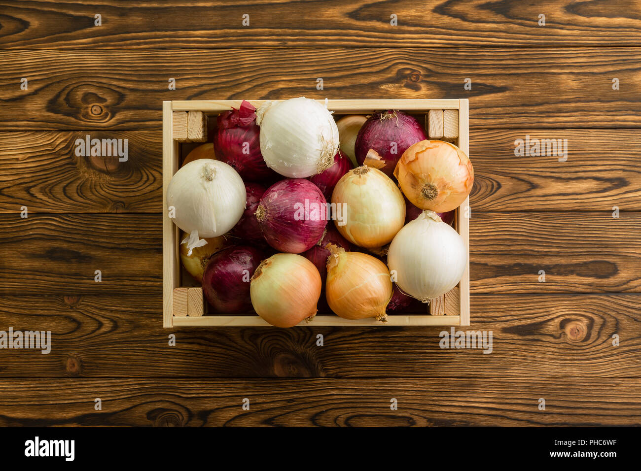 Assorted colors of fresh whole onions in a small wooden box displayed ...