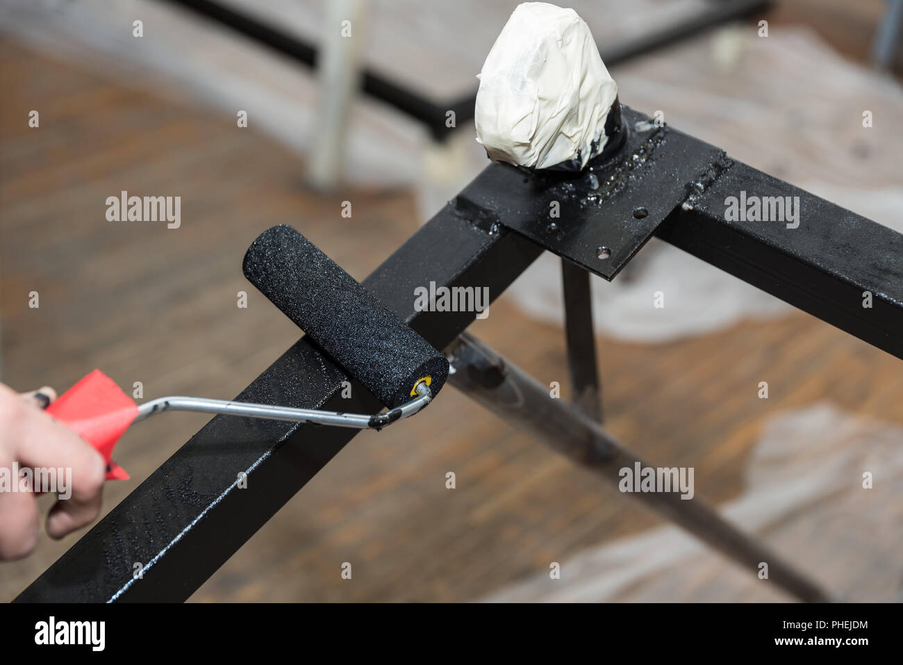 Craftsman paints metal with a paint roller black Stock Photo - Alamy