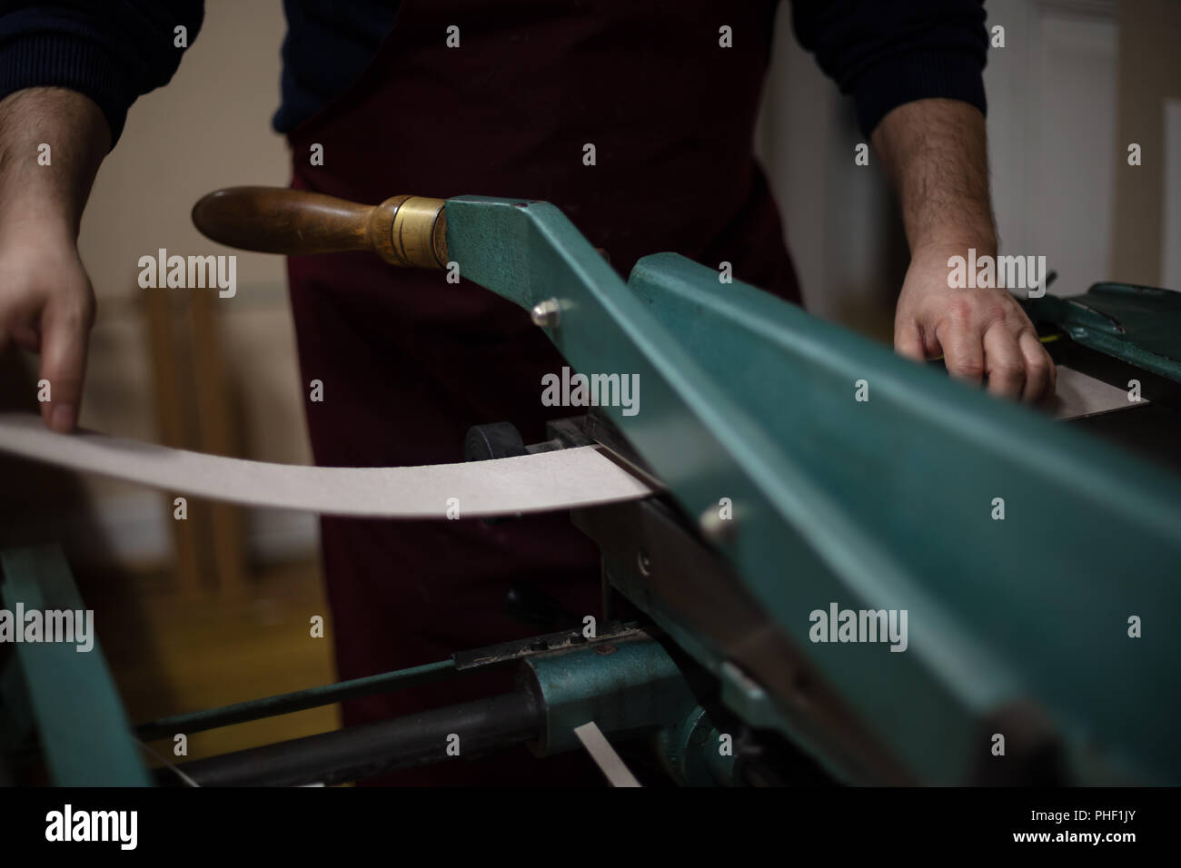 Man cutting paper and card on a large guillotine on a work table in a ...