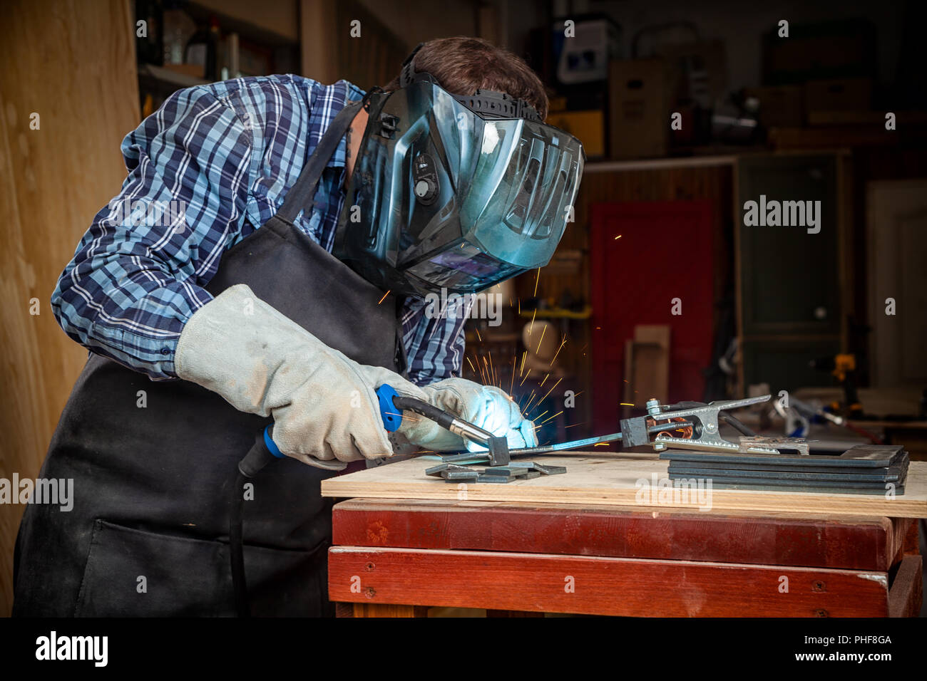 A young man welder in uniform, welding mask and welders leathers, weld ...