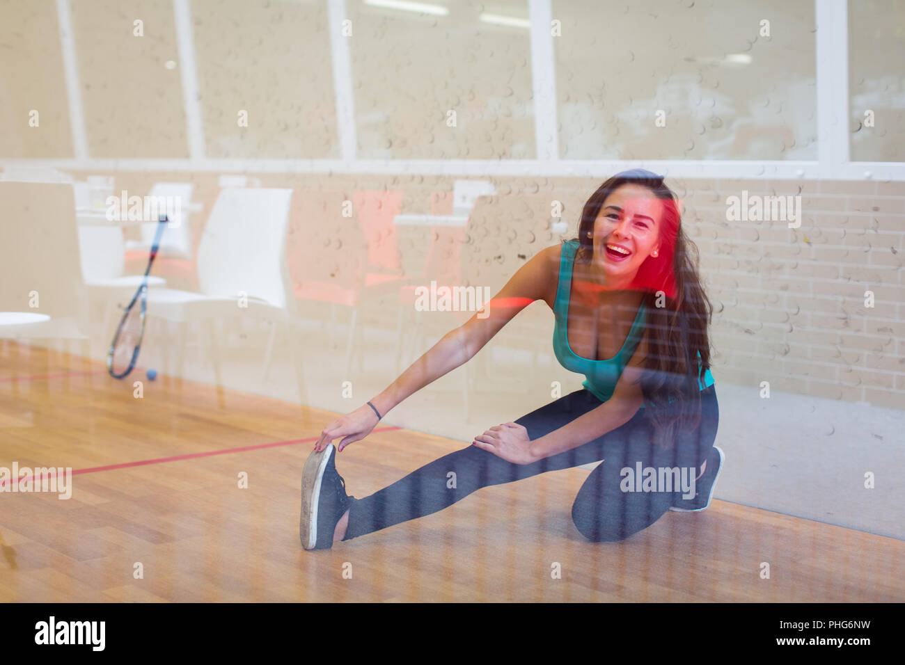 Cute young woman with a racket leaning against a wall in a squash court ...