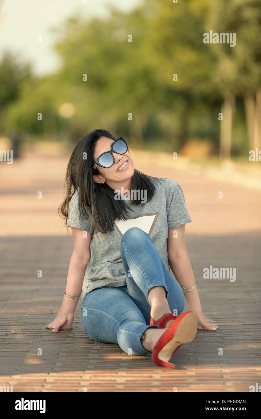 Pretty girl sitting on the path of a park looking up and smiling Stock ...