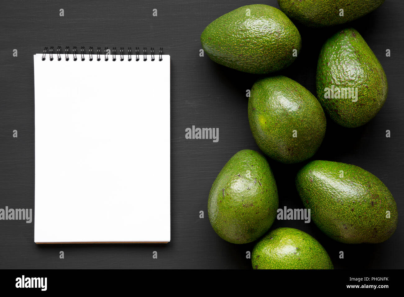 Whole avocados and blank notepad on black background, top view ...