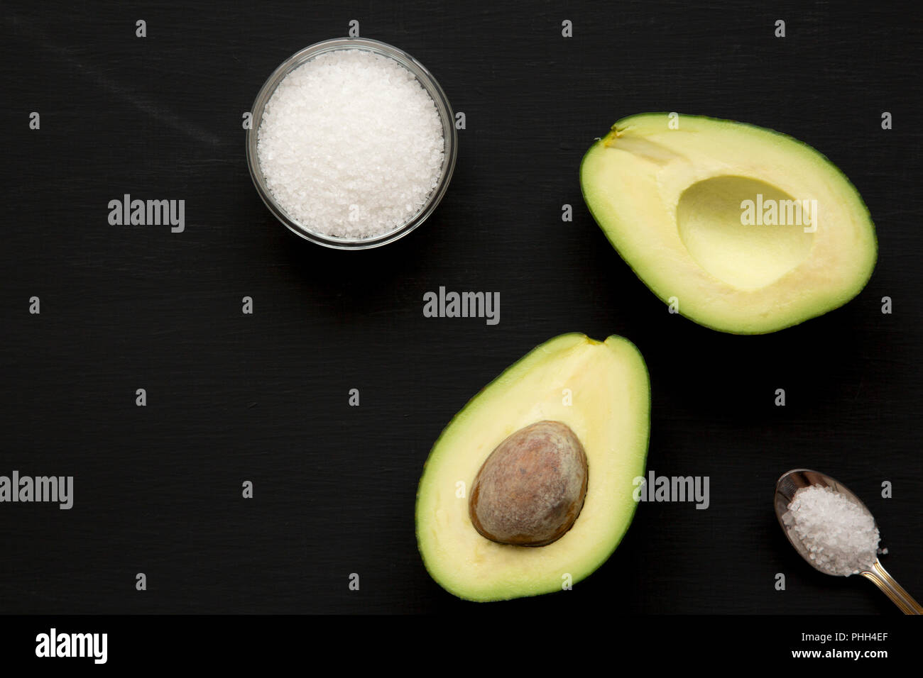 Halved avocado and sea salt over black background, top view. Flat lay ...
