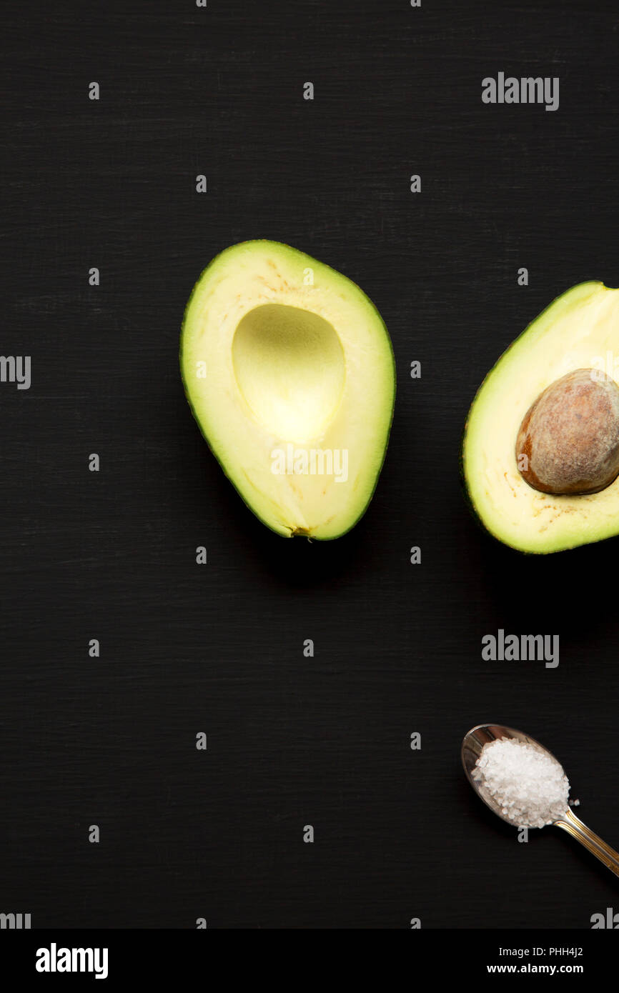 Halved avocado and sea salt on dark table, overhead view. Top view ...