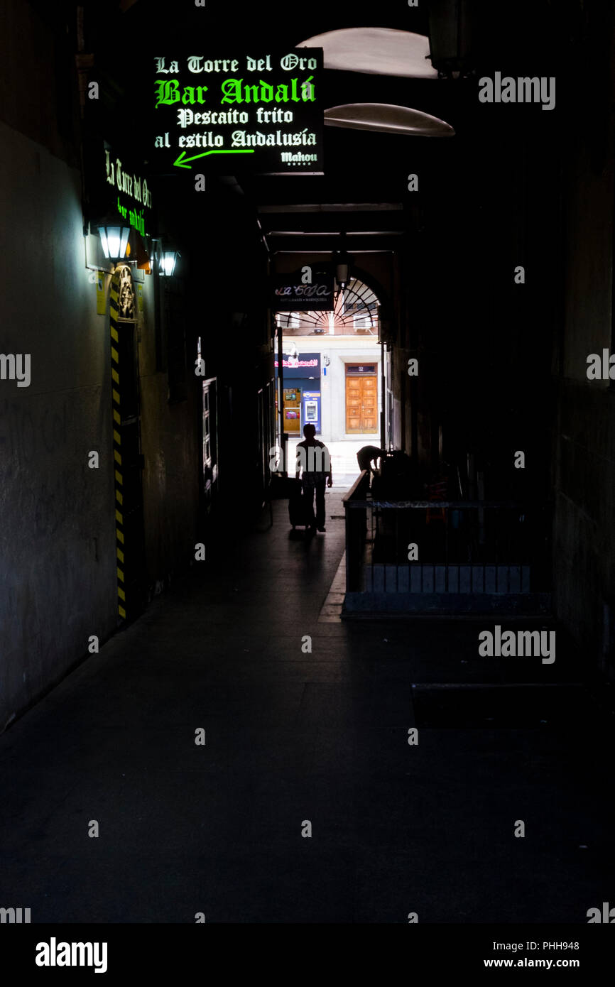 A silhouette view of a man pulling a trolley baggage in a small passage ...