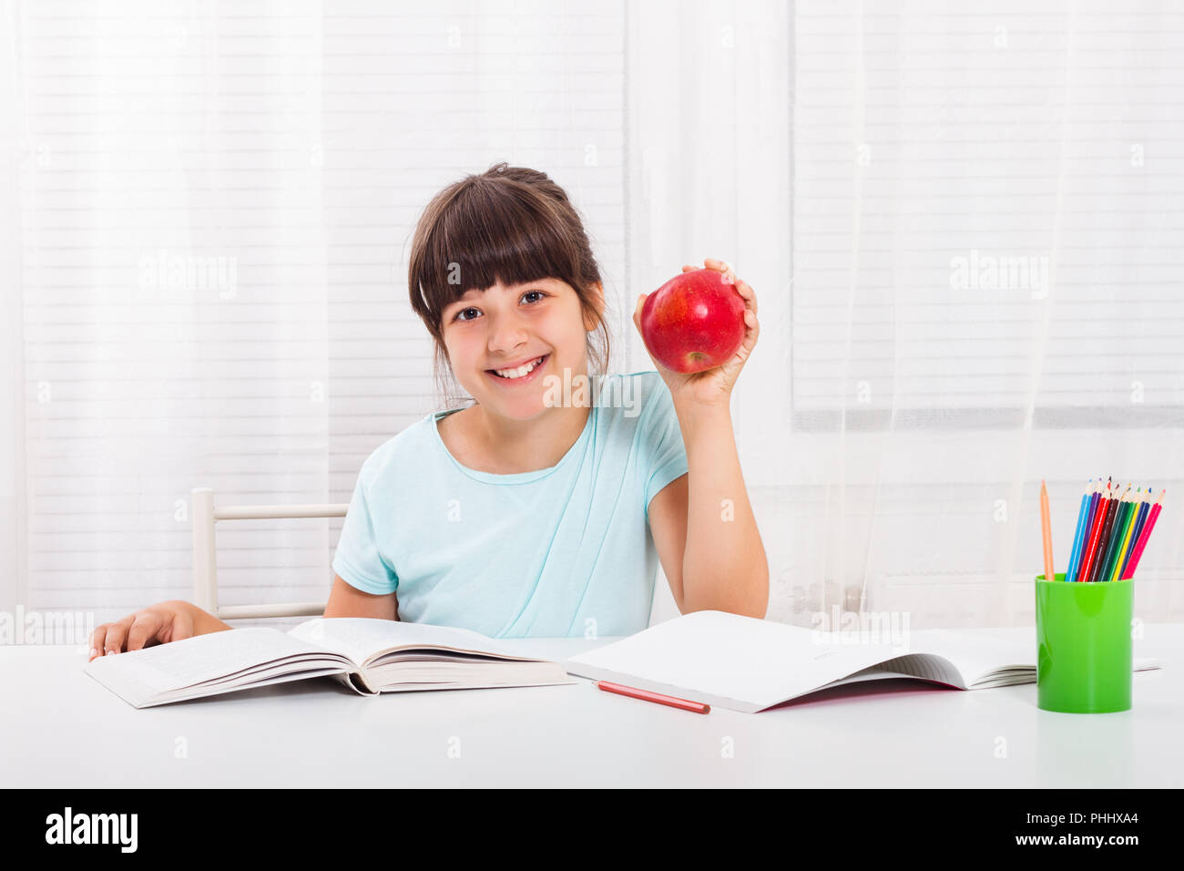 Cute little girl is having healthy snack while she is doing homework ...