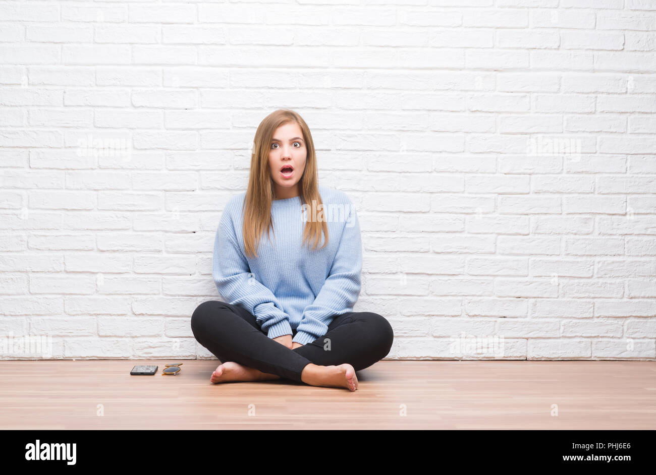 Young Adult Woman Sitting On The Floor In Autumn Over White Brick Wall