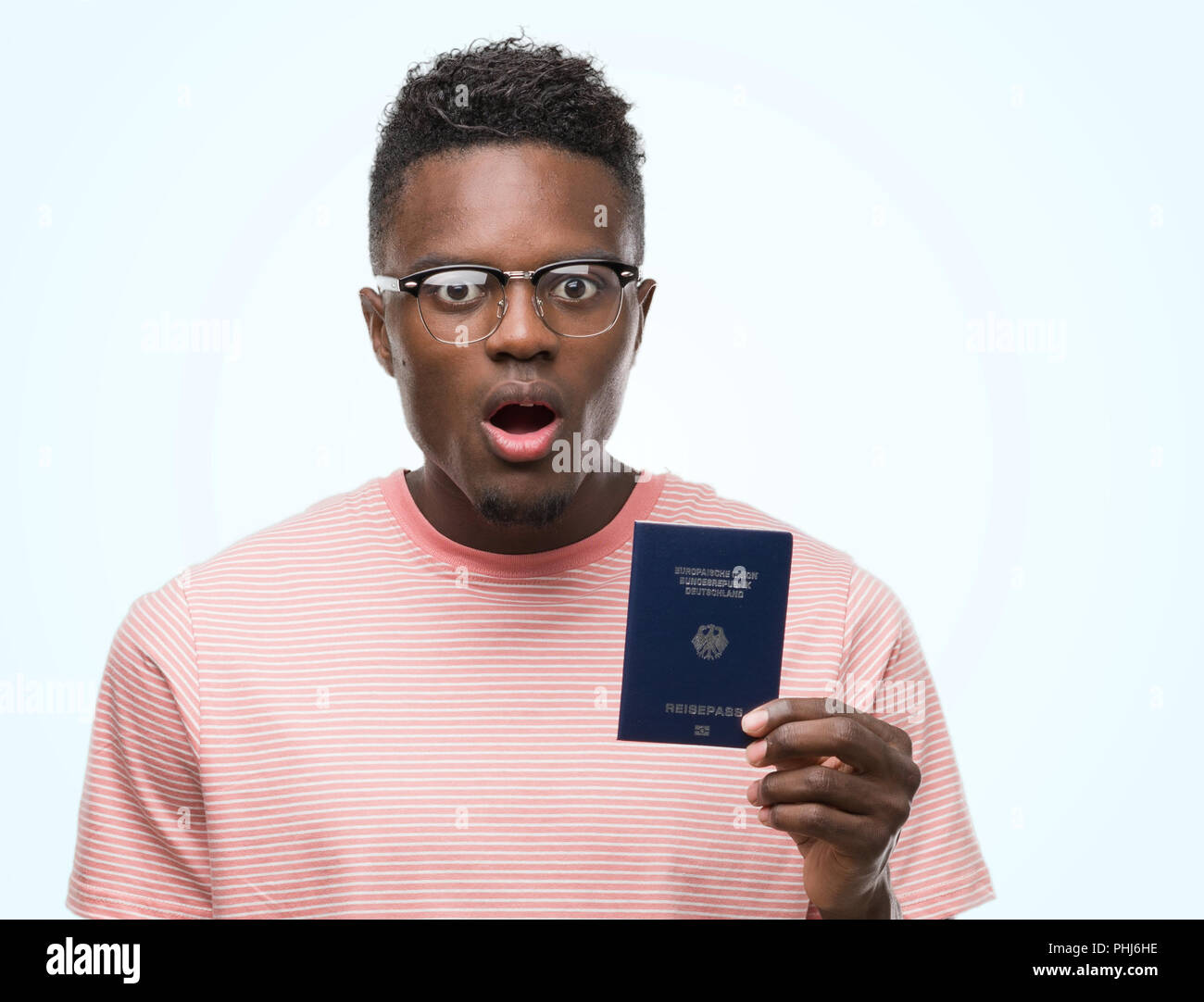 Young african american man holding german passport scared in shock with ...