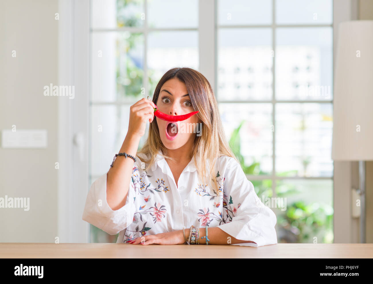 Young woman at home eating red hot chili pepper scared in shock with a ...