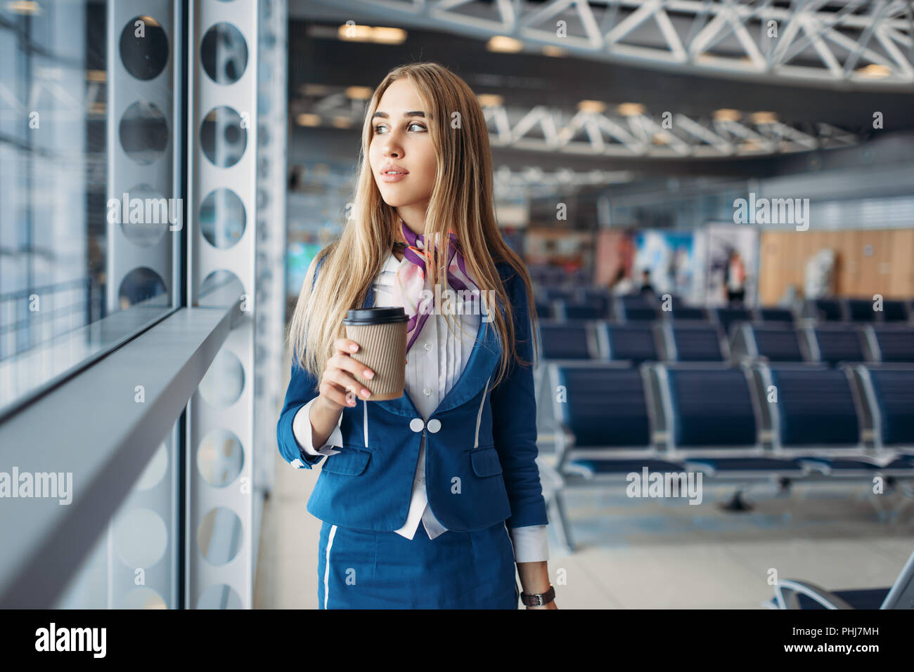 Stewardess with suitcase and coffee against window in airport. Air ...