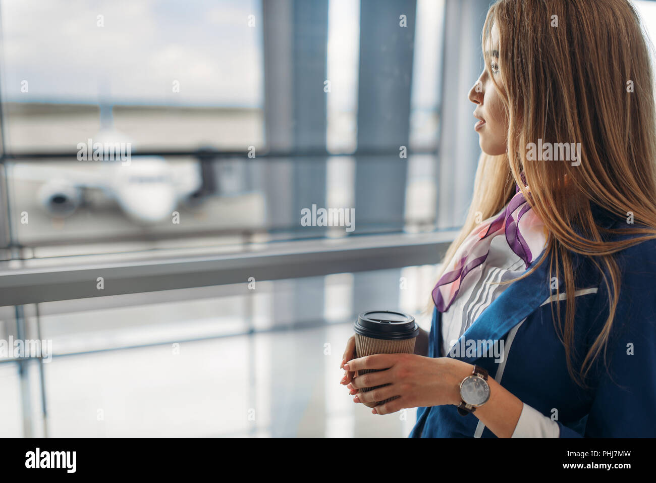 Stewardess with coffee and suitcase sitting on seat in waiting area in ...