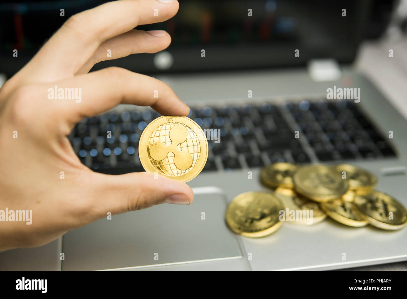 Male businessman hand holding Ripple coin on a background of laptop ...