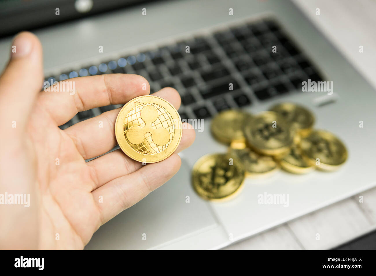 Male businessman hand holding Ripple coin on a background of laptop ...