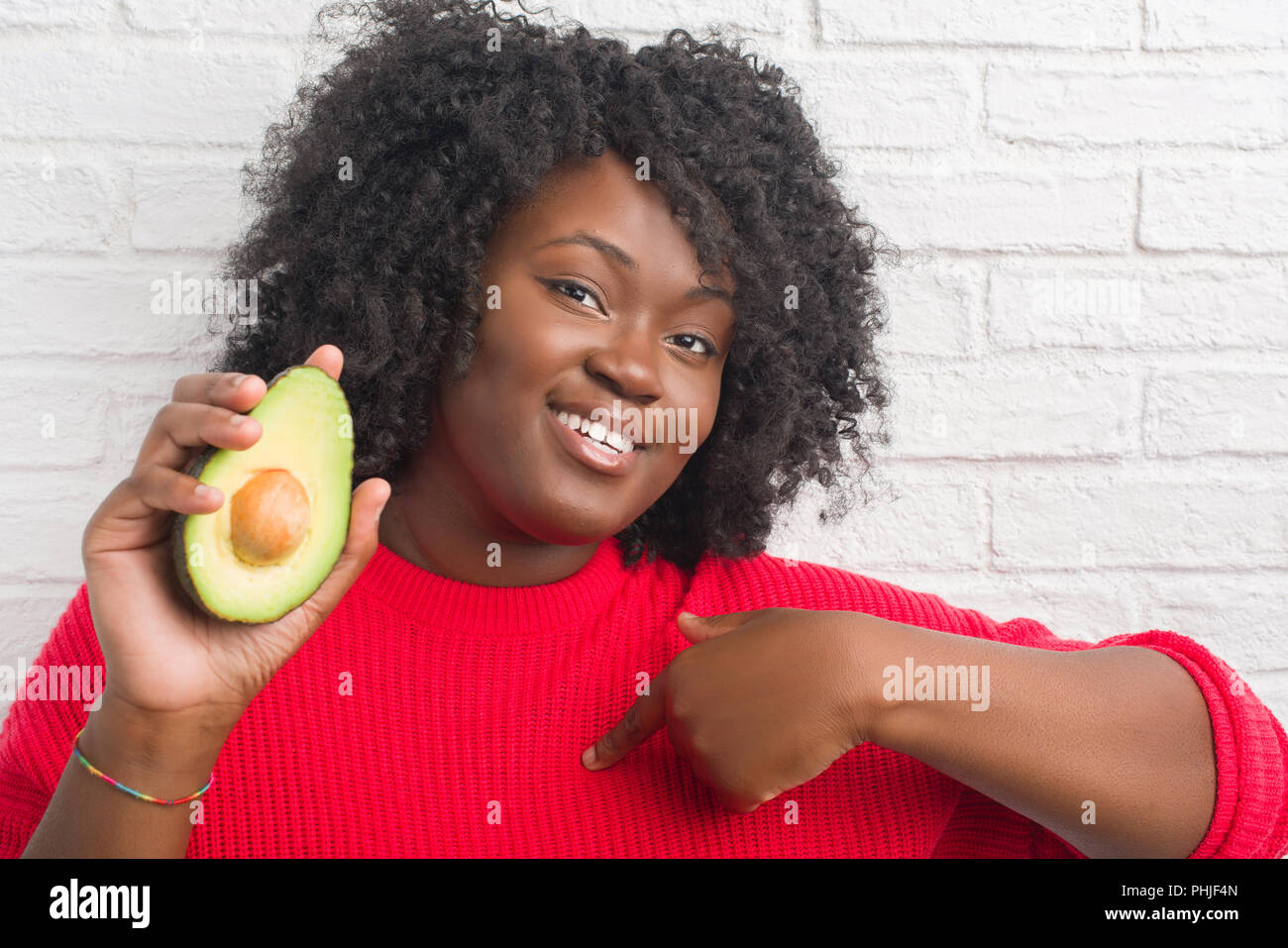 Young african american woman over white brick wall eating avocado with ...