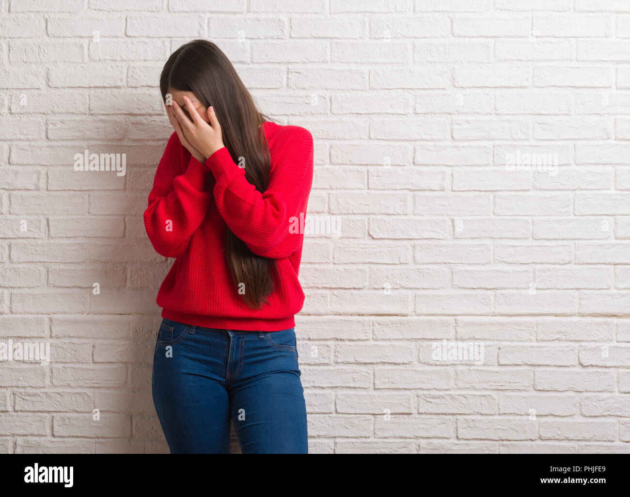 Young Chinese woman over brick wall with sad expression covering face ...