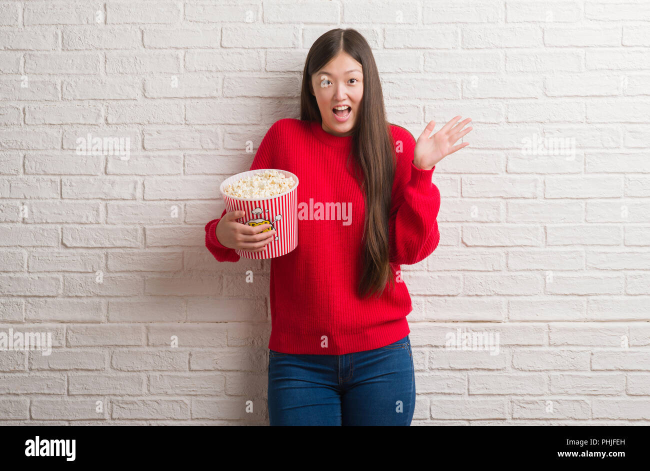 Young Chinese woman over brick wall eating pop corn very happy and ...