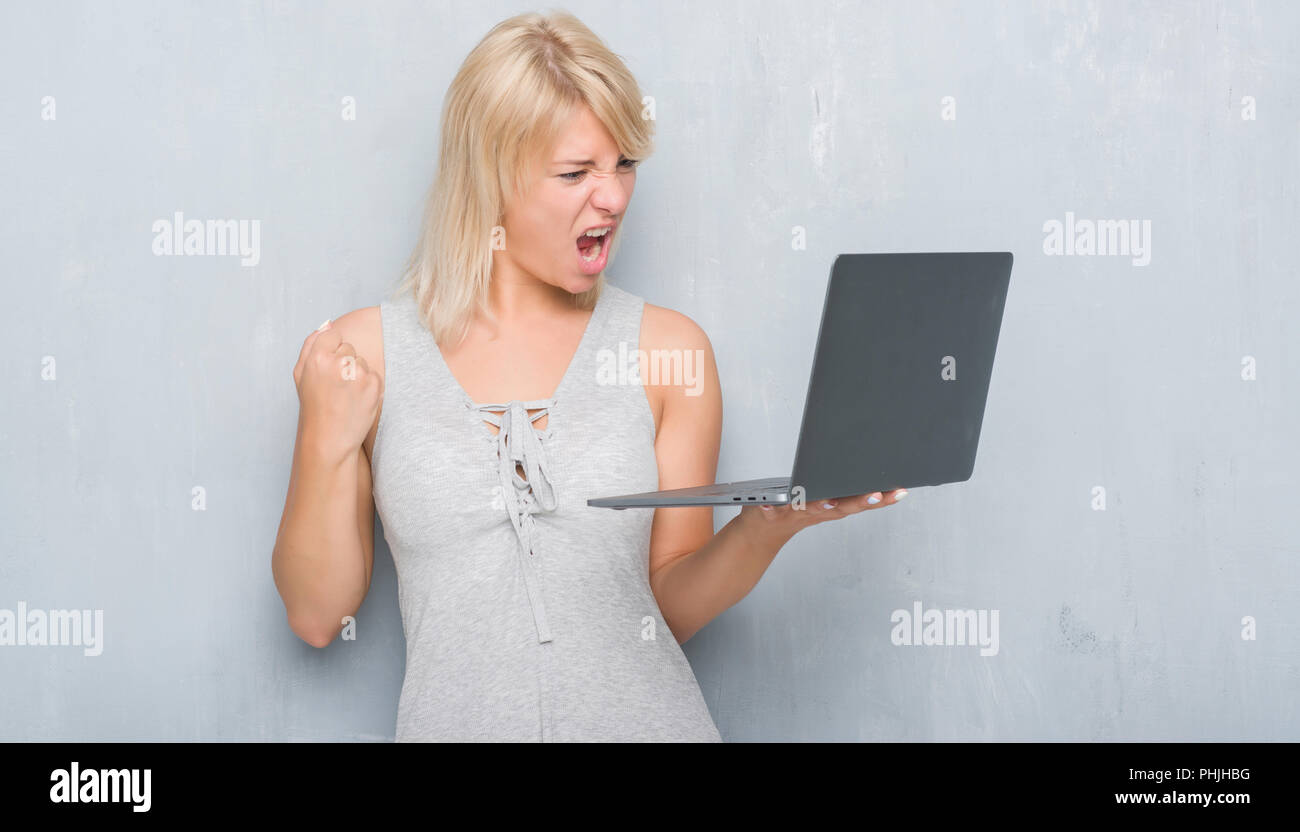 Adult caucasian woman over grunge grey wall using computer laptop ...