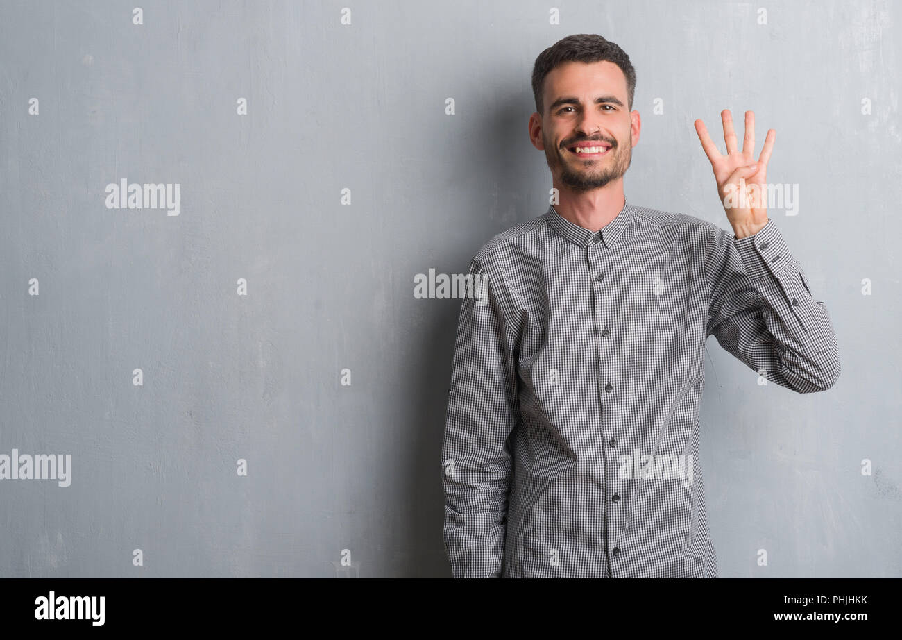 Young adult man standing over grey grunge wall showing and pointing up ...