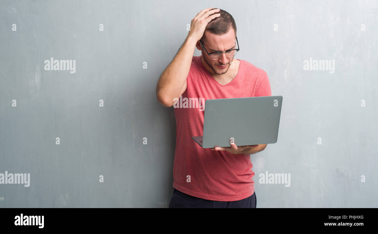 Young caucasian man over grey grunge wall using computer laptop ...