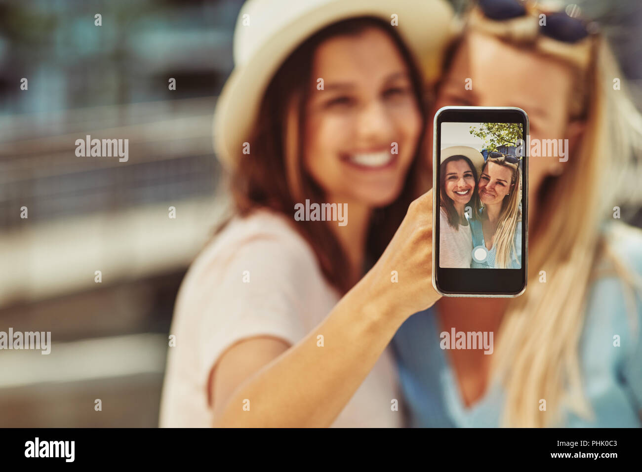 Two smiling young female friends taking selfies with a cellphone while ...