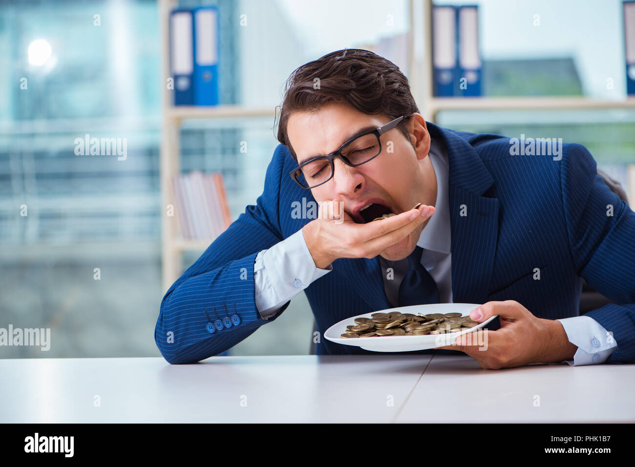 Funny businessman eating gold coins in office Stock Photo - Alamy