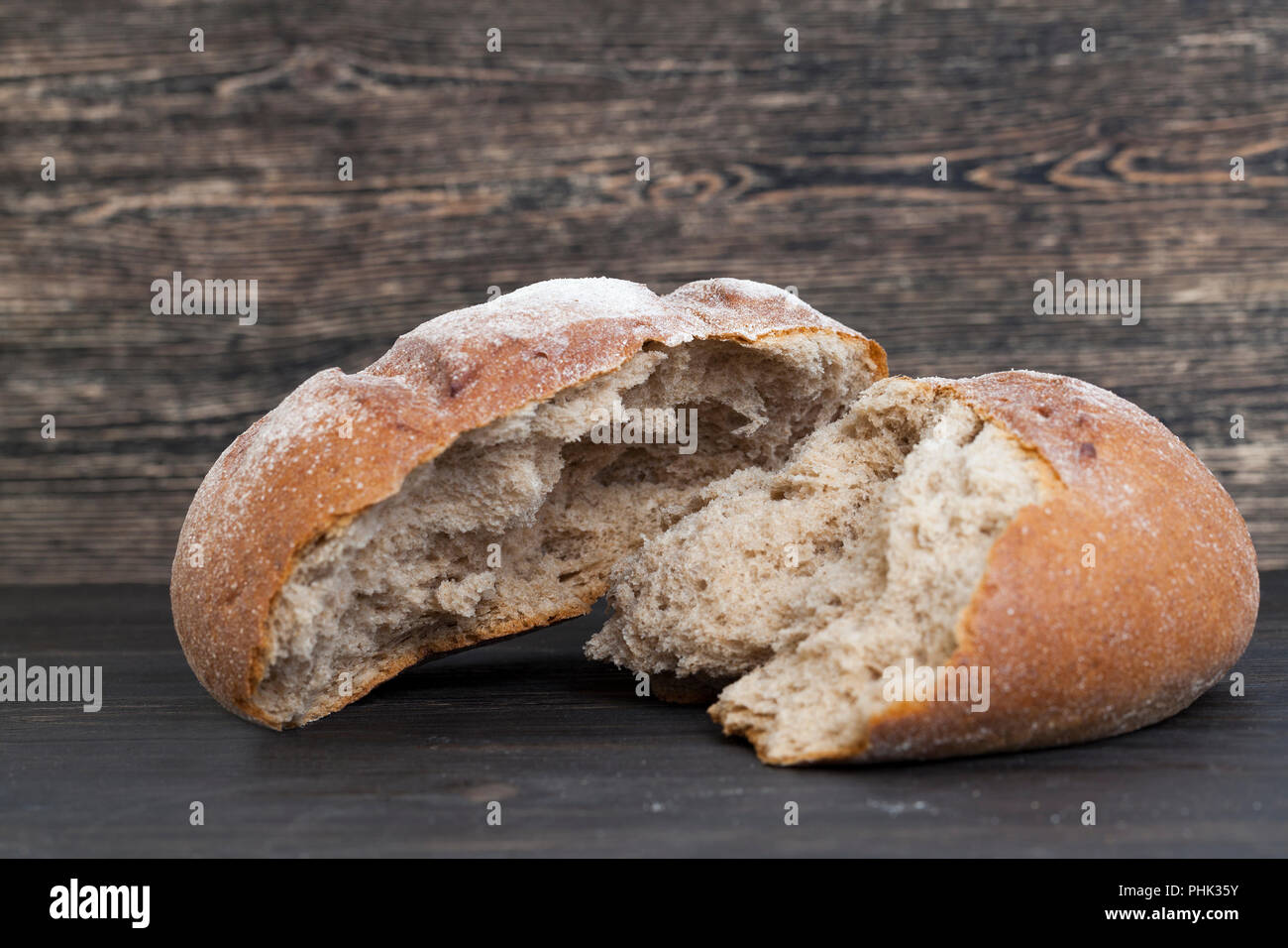 broken into half a loaf of fresh bread in black, closeup in the kitchen ...