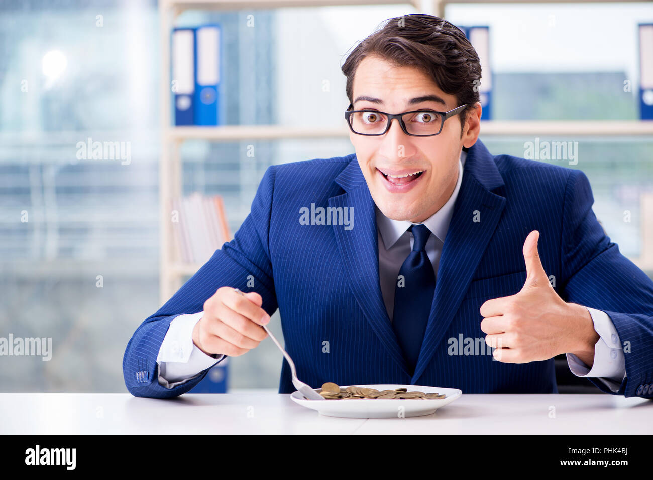 Funny businessman eating gold coins in office Stock Photo - Alamy