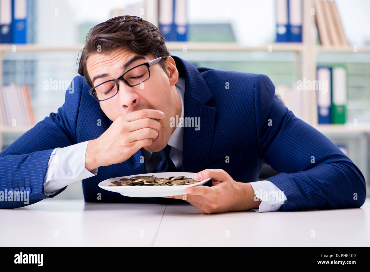 Funny businessman eating gold coins in office Stock Photo - Alamy
