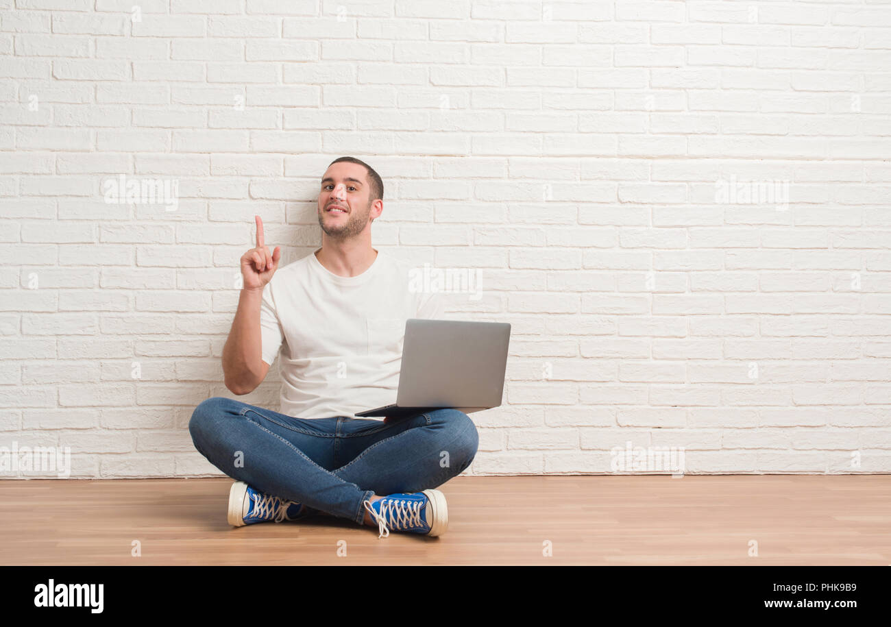 Young caucasian man sitting over white brick wall using computer laptop ...