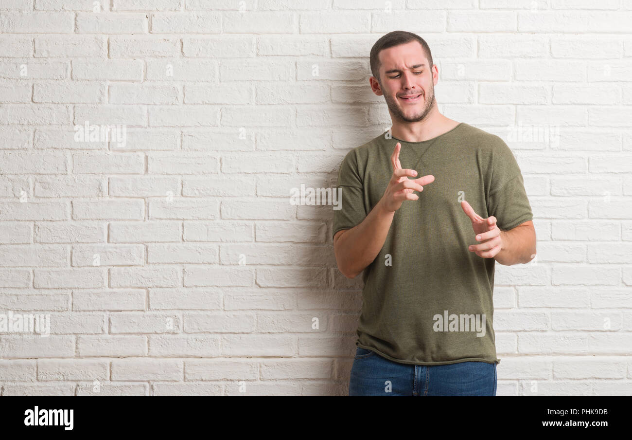 Young caucasian man standing over white brick wall disgusted expression ...