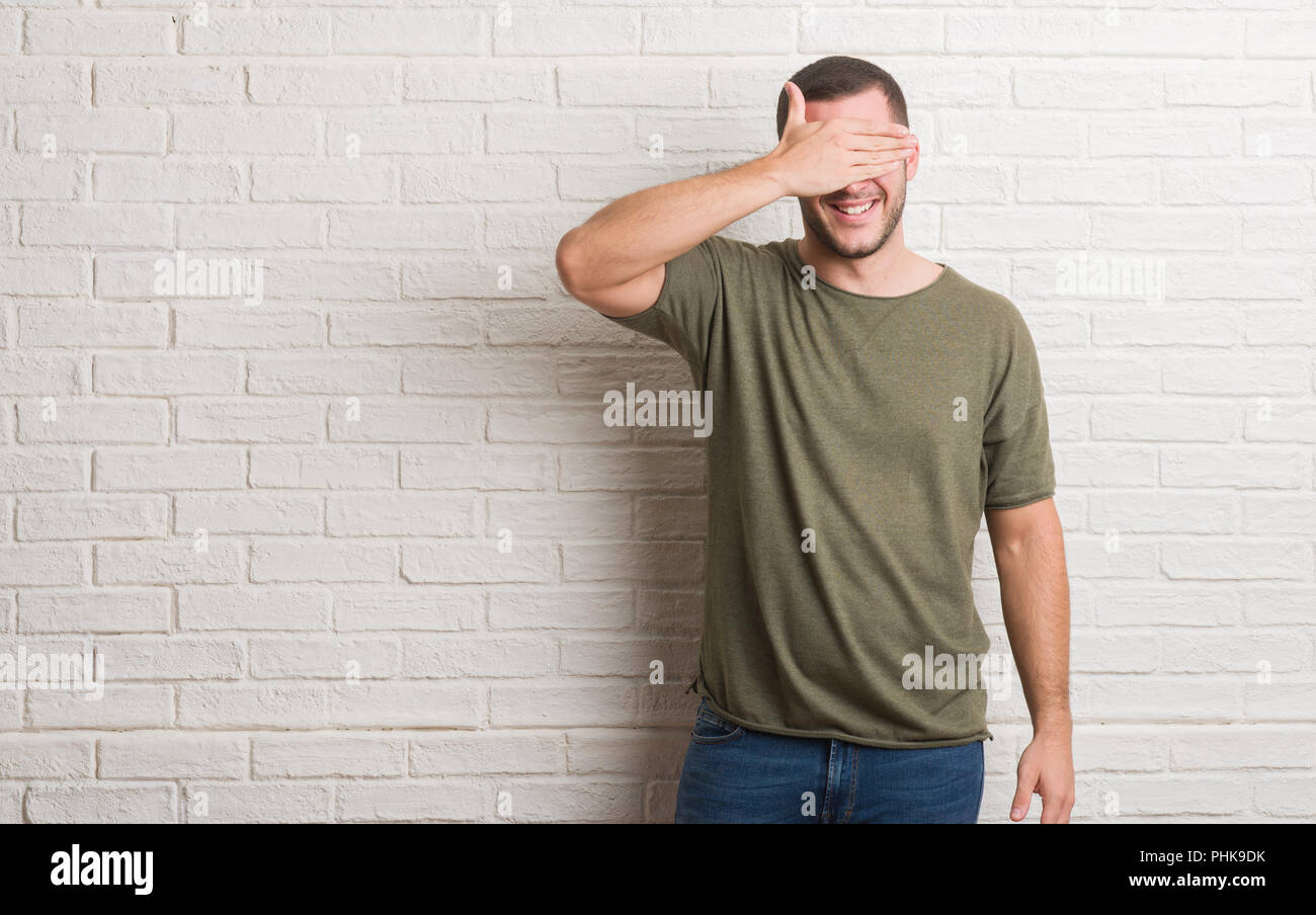 Young caucasian man standing over white brick wall smiling and laughing ...