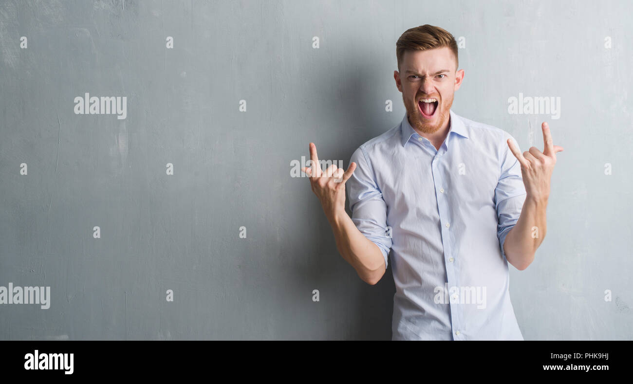 Young redhead business man over grey grunge wall shouting with crazy ...